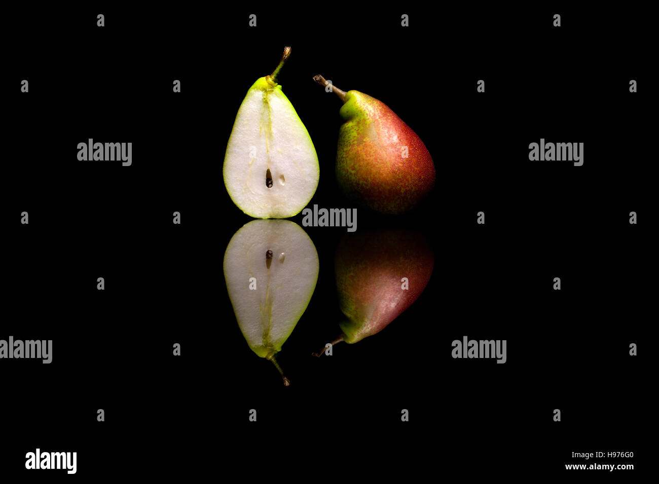 One cut in half and one whole red and green pears isolated on black ...