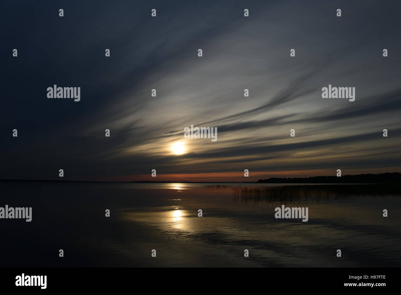 Sunset in the cloudy haze of sun ray glides over the surface of water ...