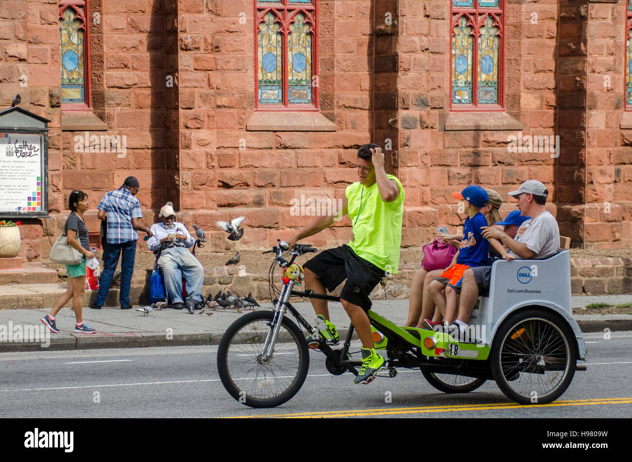 A family riding in a bicycle rickshaw passes a man feeding many pigeons ...