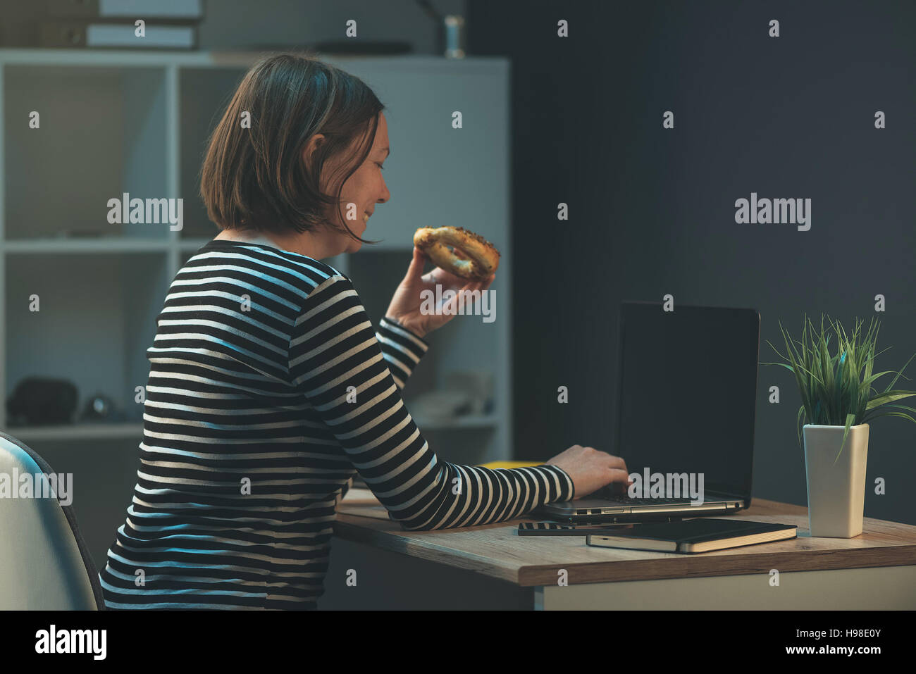 Business woman eating baked snack over office laptop computer. Young ...