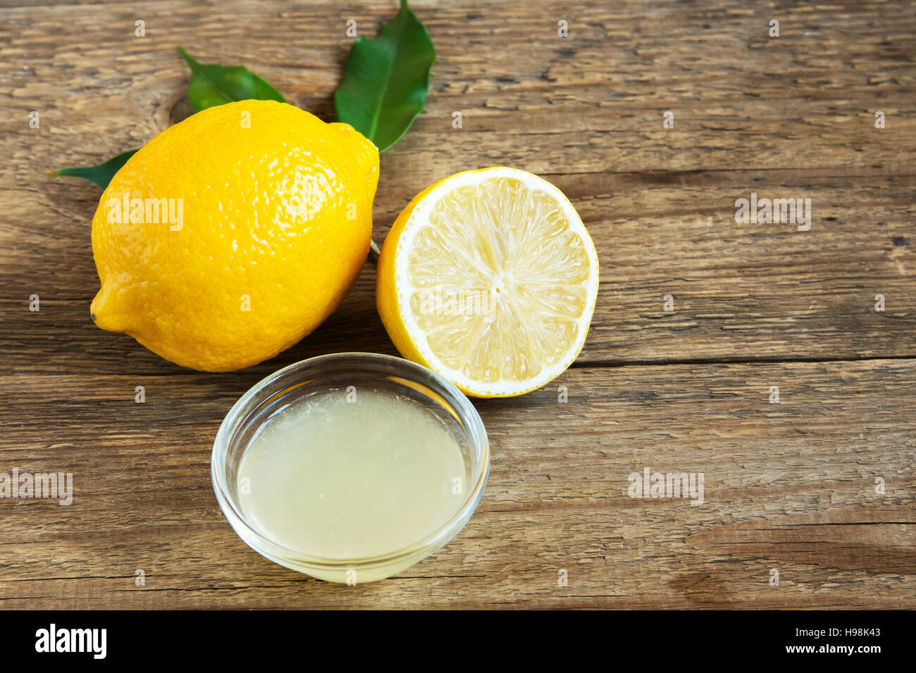Fresh lemon juice in small bowl and lemons over rustic wooden ...