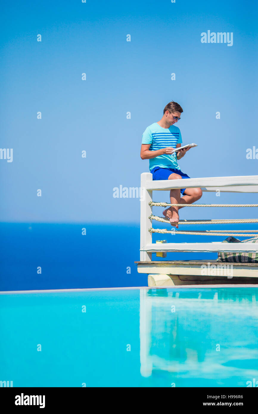 Caucasian guy relaxing near pool with amazing view and reading book in ...