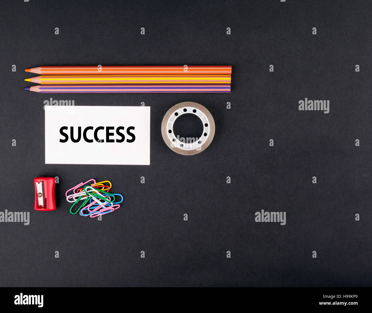 SUCCESS. Top view of a black ofice desk. Colored pencils, business card ...