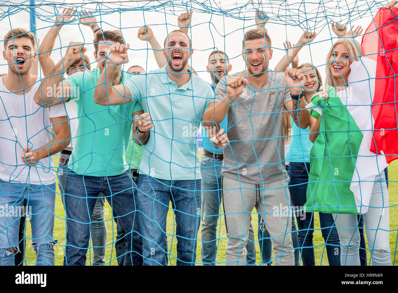 Group of soccer fans behind net cheering Stock Photo - Alamy