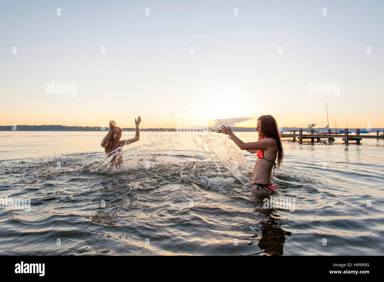 Two young women splashing each other in lake Stock Photo - Alamy