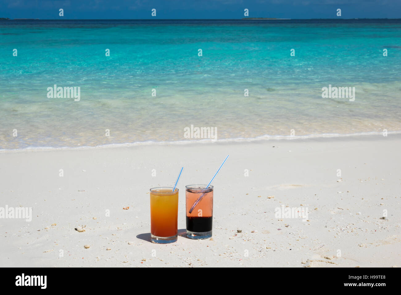 Two colorful cocktails laying on white sand, small corals covered beach ...