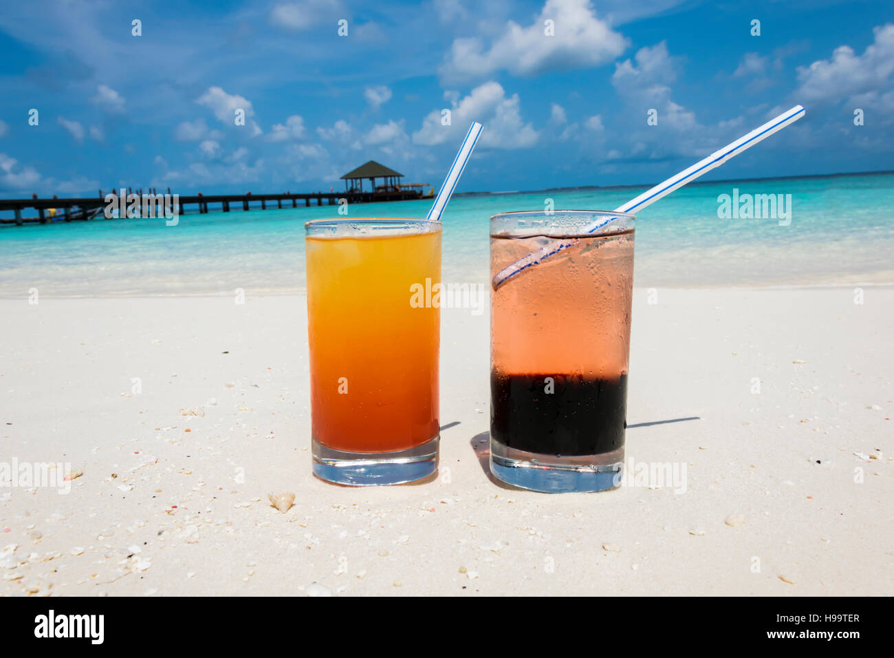 Two colorful cocktails laying on white sand, small corals covered beach ...