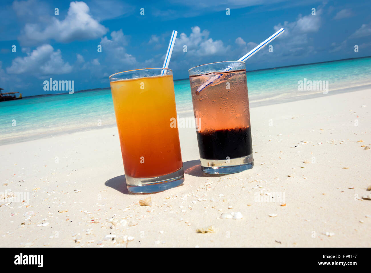 Two colorful cocktails laying on white sand, small corals covered beach ...