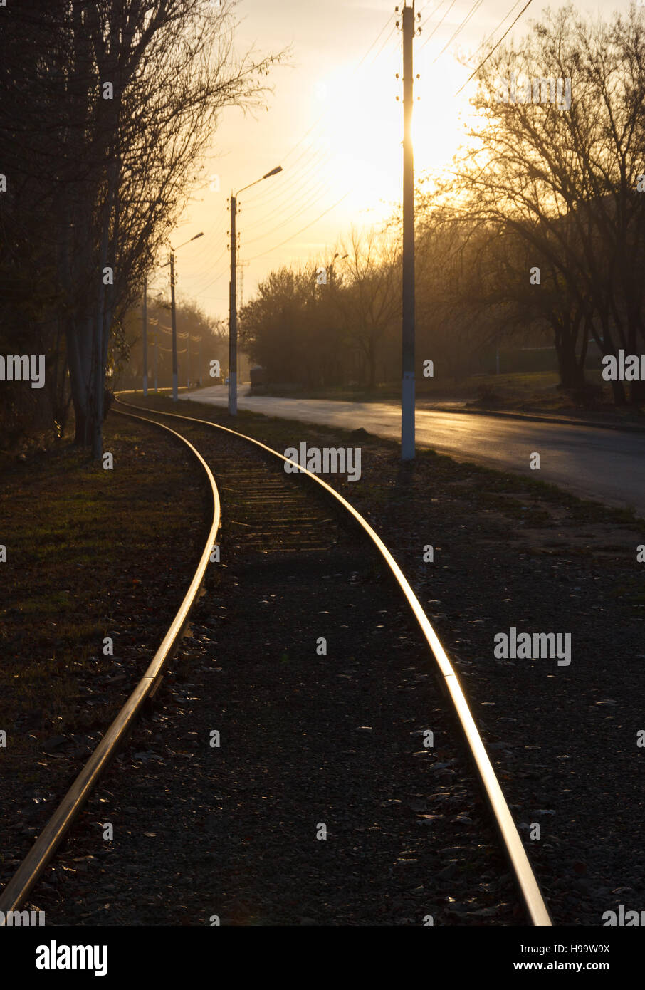 Railway track running along a road at sunset Stock Photo - Alamy