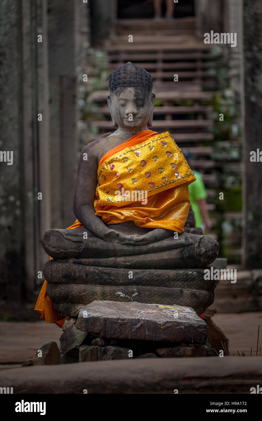 Stone statue of Buddha wrapped with saffron and gold silk at Ta Prohm ...