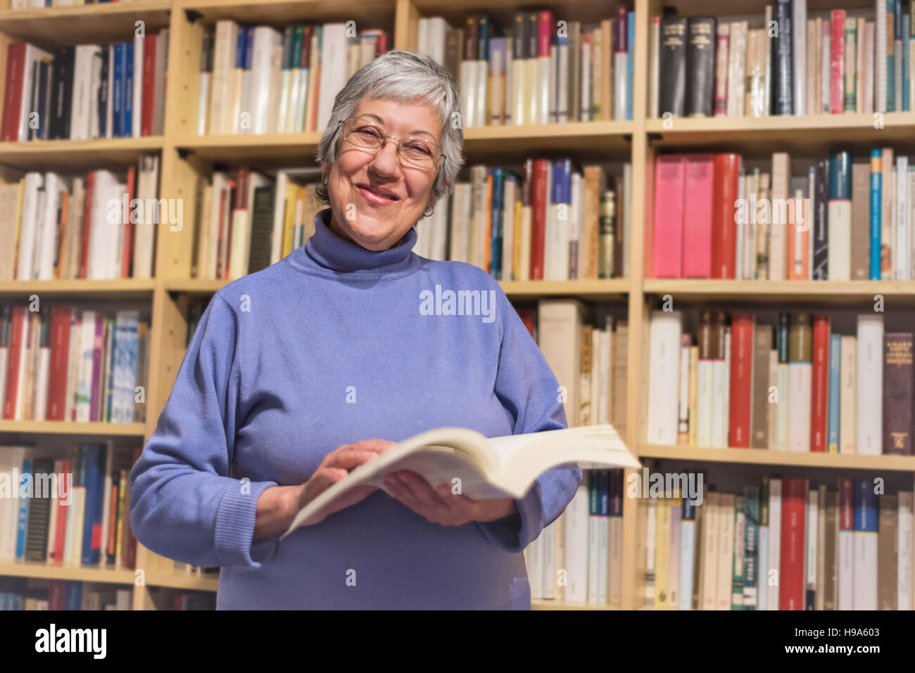 Senior woman reading a book at home. Happy expression. A blurry library ...