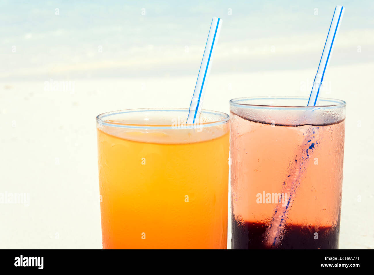 Two colorful cocktails laying on white sand, small corals covered beach ...