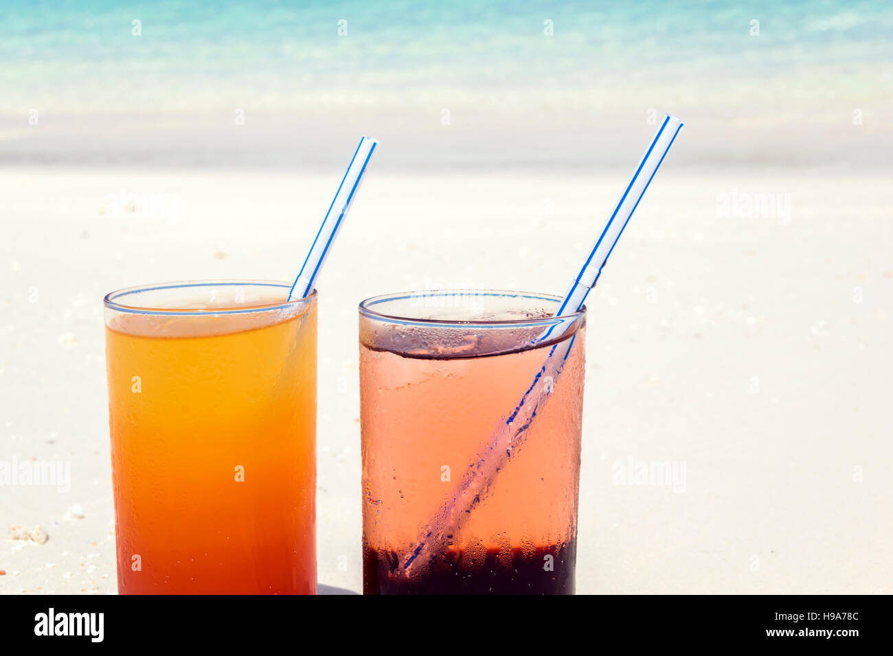 Two colorful cocktails laying on white sand, small corals covered beach ...