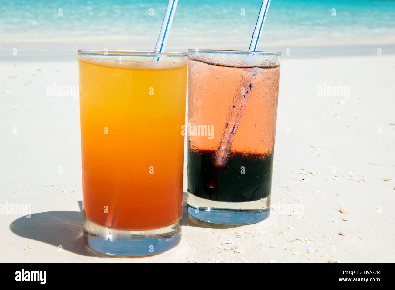 Two colorful cocktails laying on white sand, small corals covered beach ...