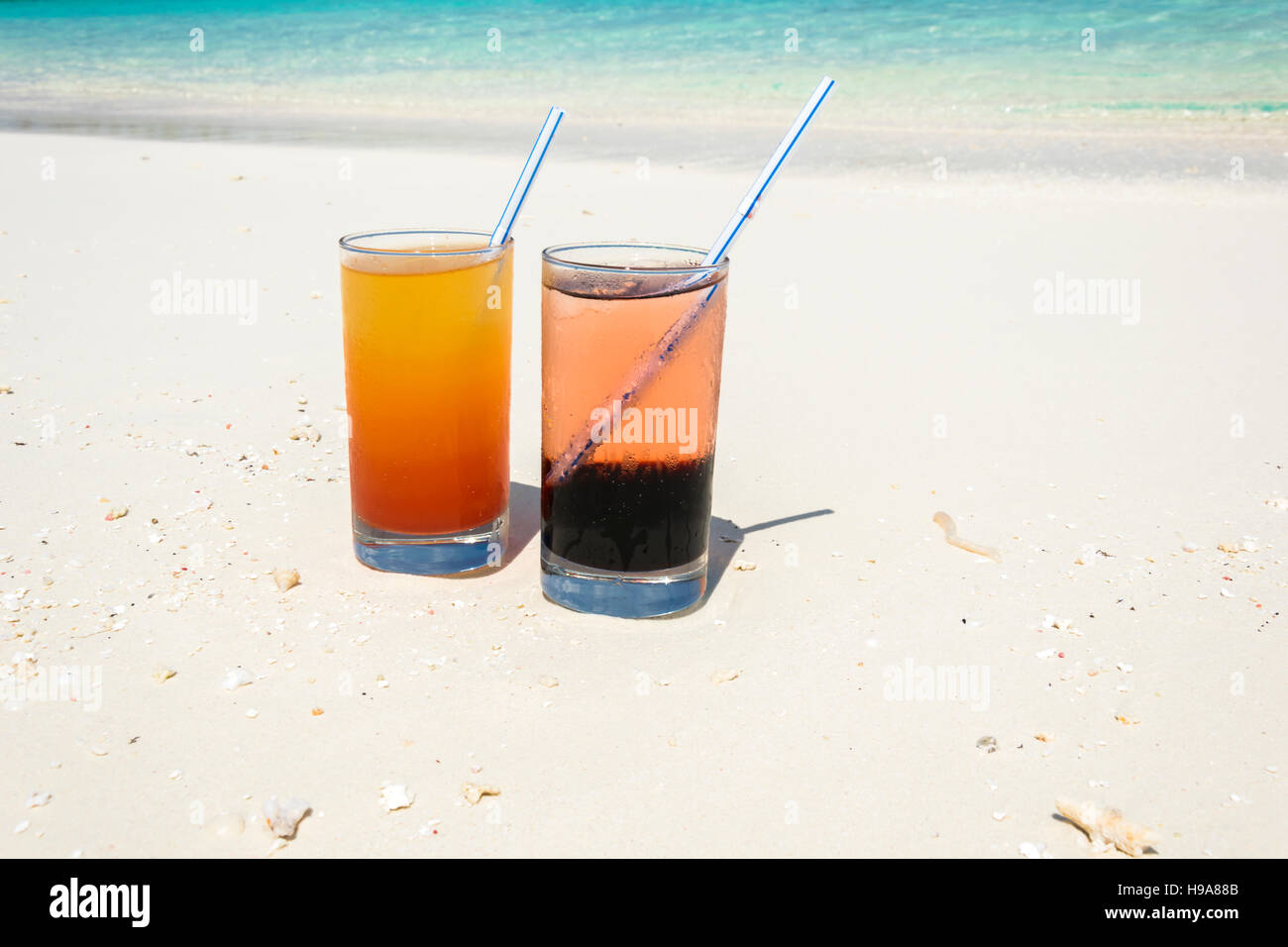 Two colorful cocktails laying on white sand, small corals covered beach ...