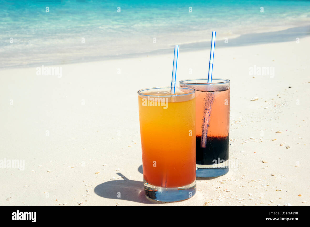 Two colorful cocktails laying on white sand, small corals covered beach ...
