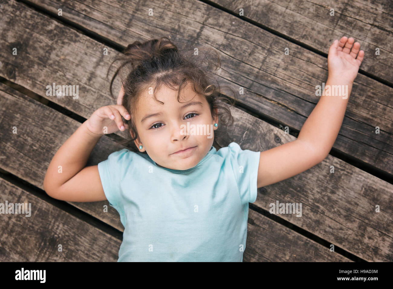 A girl laying on wooden floor looking at camera. Horizontal outdoors ...