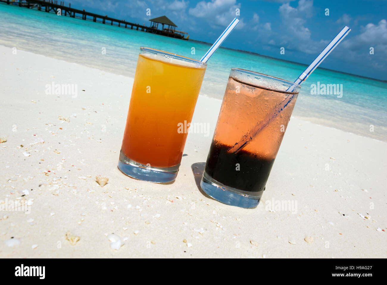 Two colorful cocktails laying on white sand, small corals covered beach ...