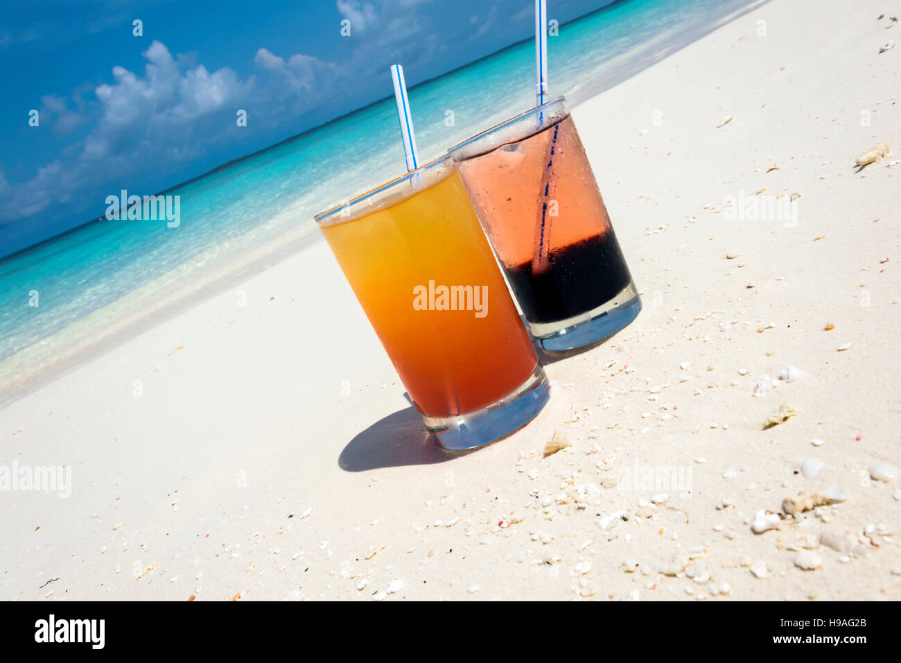 Two colorful cocktails laying on white sand, small corals covered beach ...