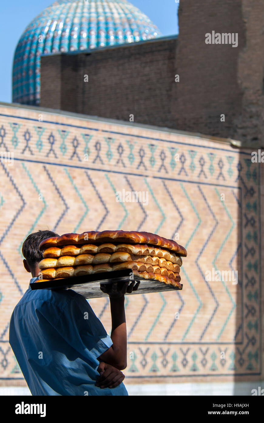 A young man carrying a tray of freshly baked bread past a minaret in ...