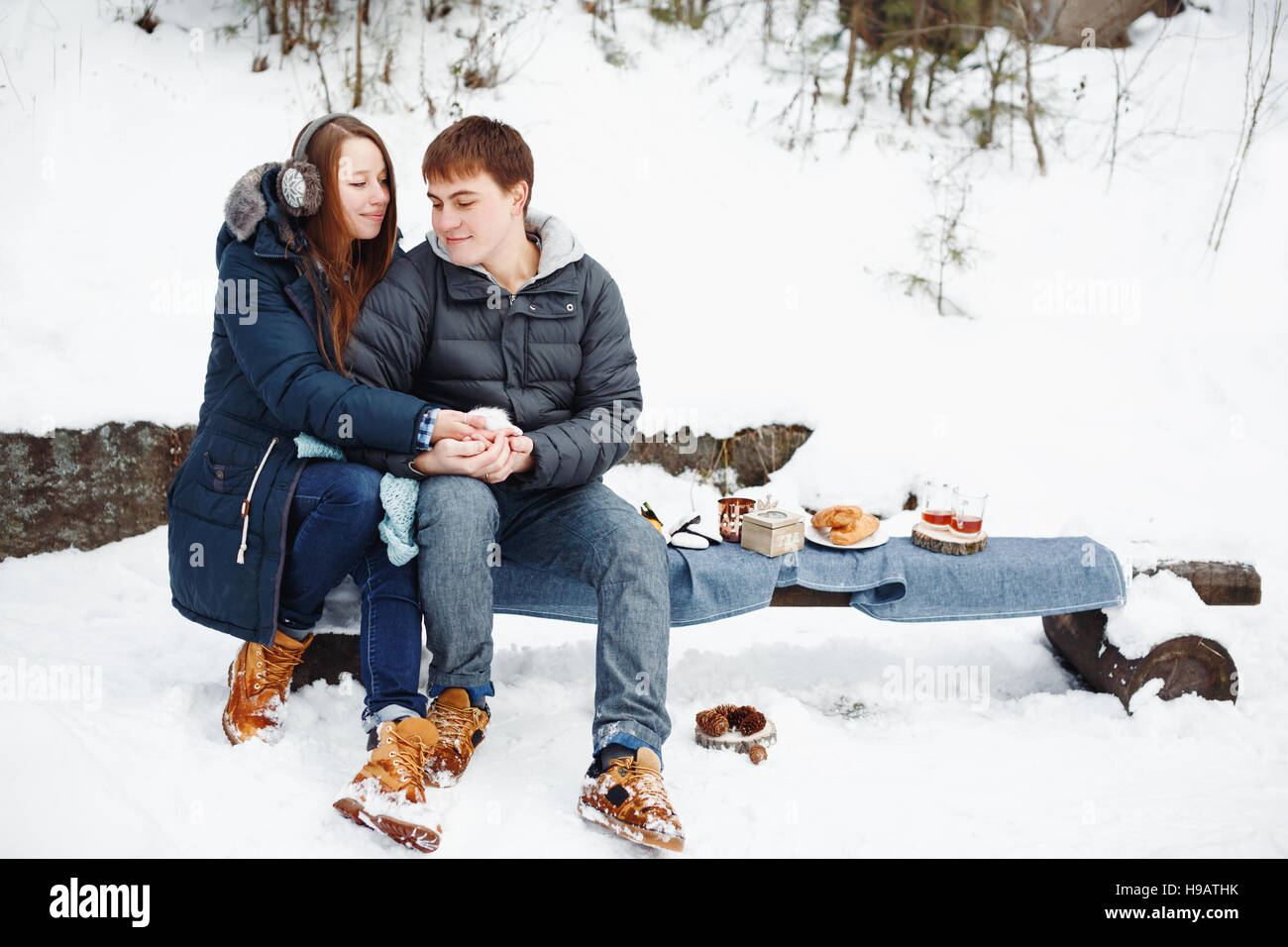 Couple in love drinking hot tea outside, winter forest with wooden ...