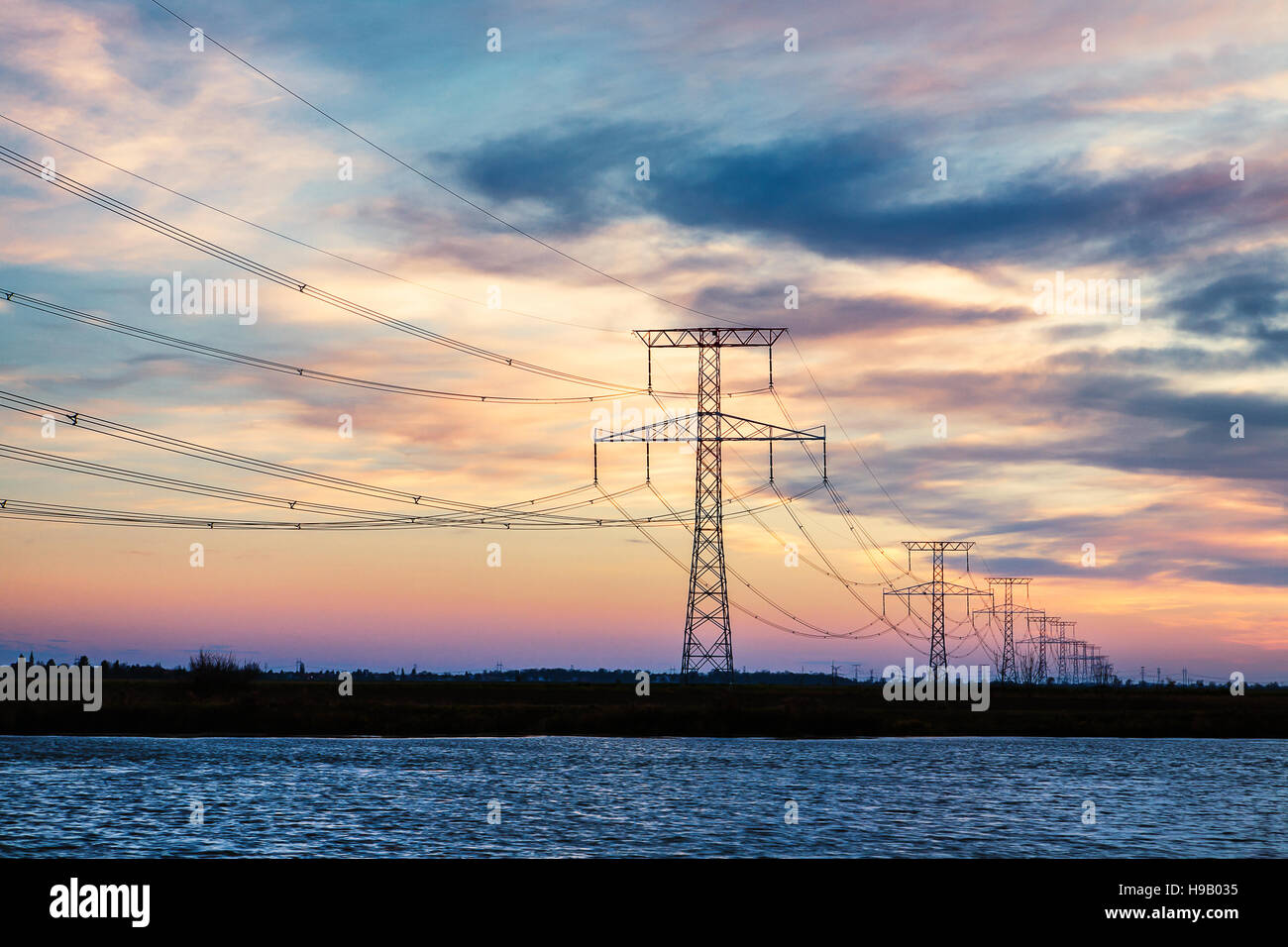 High voltage power lines over river at sunset Stock Photo - Alamy