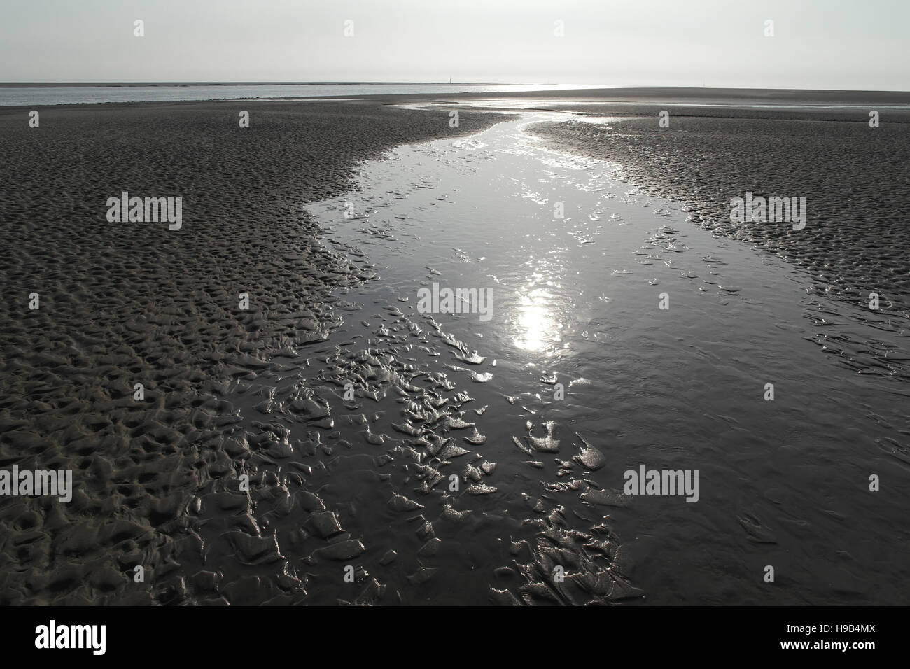 White sun reflecting in water channel crossing sand beach expanse ...