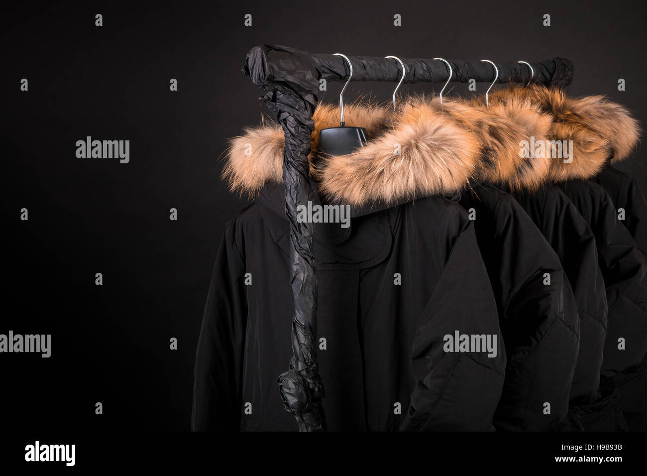 Black coats, jacket with fur on hood hanging on clothes rack. Black ...