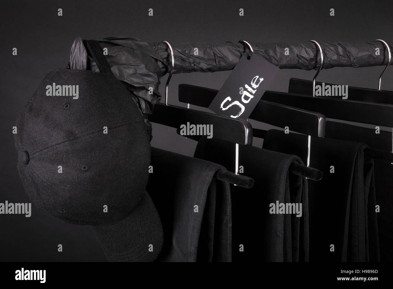 Sale sign. Black cap and pant, jeans hanging on clothes rack on black ...