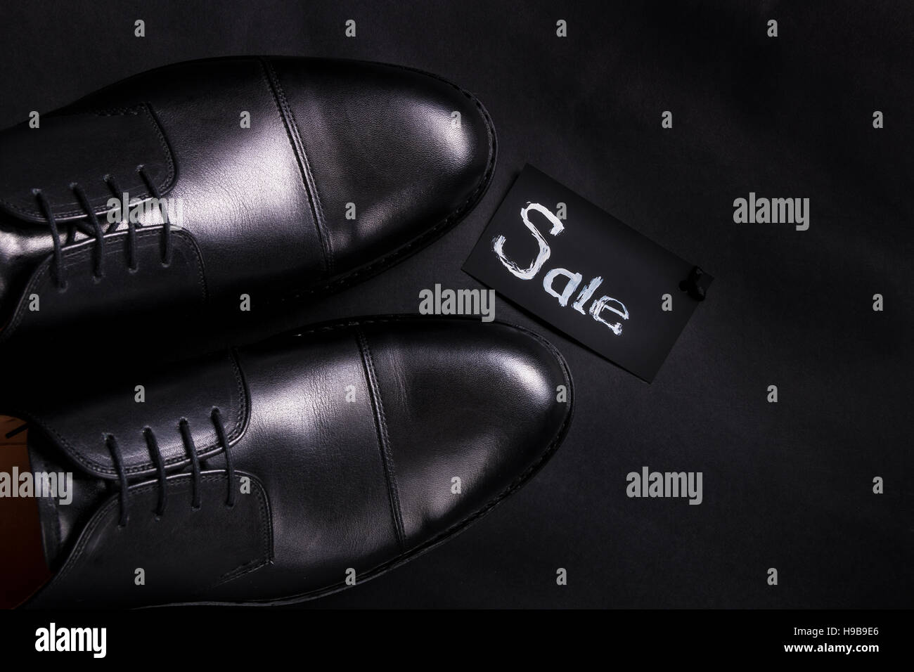 Sale sign. Black oxford shoes on black background. Top view. Copy space ...
