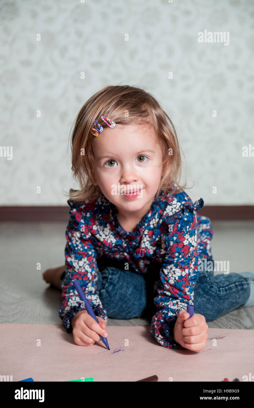 Child painting, sitting on the floor looking at the camera near crayons ...