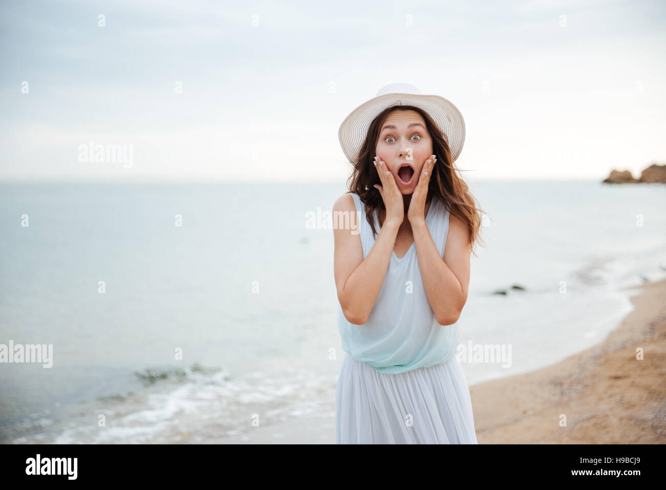 Amazed shocked young woman in hat standing and shouting in the beach ...