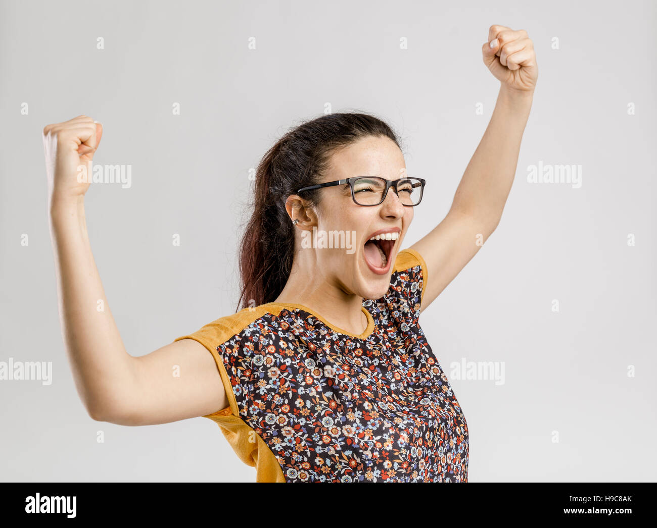 Beautiful and happy woman with both arms up, isolated over a gray ...