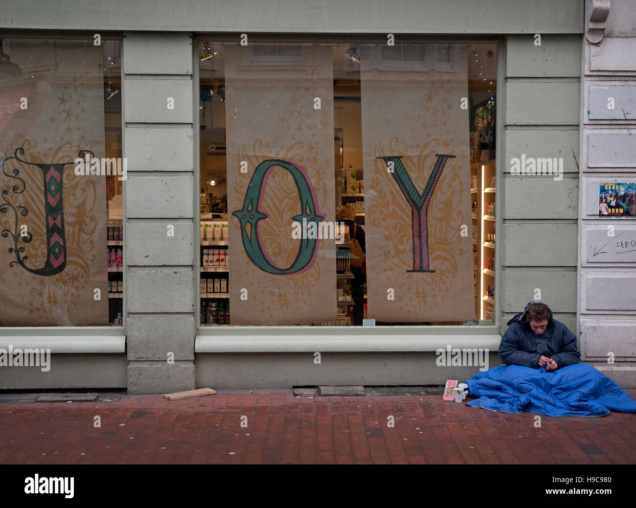 A homeless man sits on the pavement by a joyful shop window display in ...