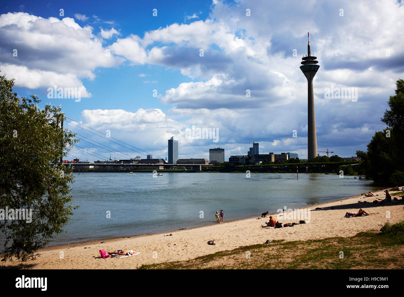 People sunbathing on the banks of the river Rhein, with the Rheinturm ...