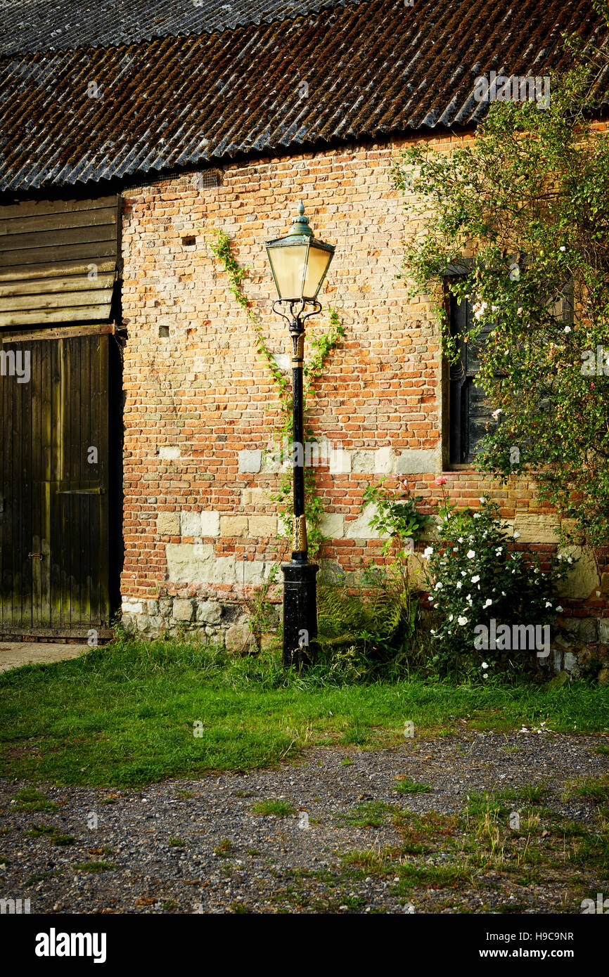 An old street lamp against a red bricked barn with a moss covered ...