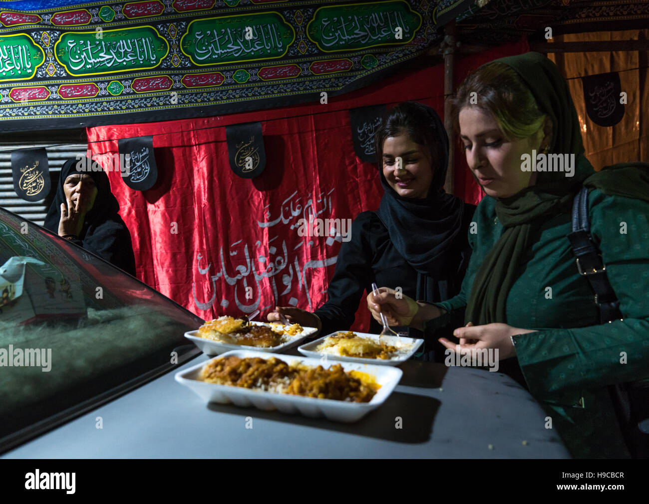 Women eating nazri charity food given during muharram on a car hood ...