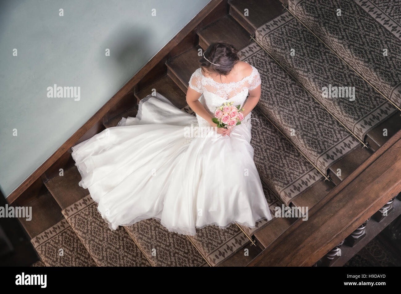 Bride sat on the stairs with her wedding dress fanned out. Looking down ...