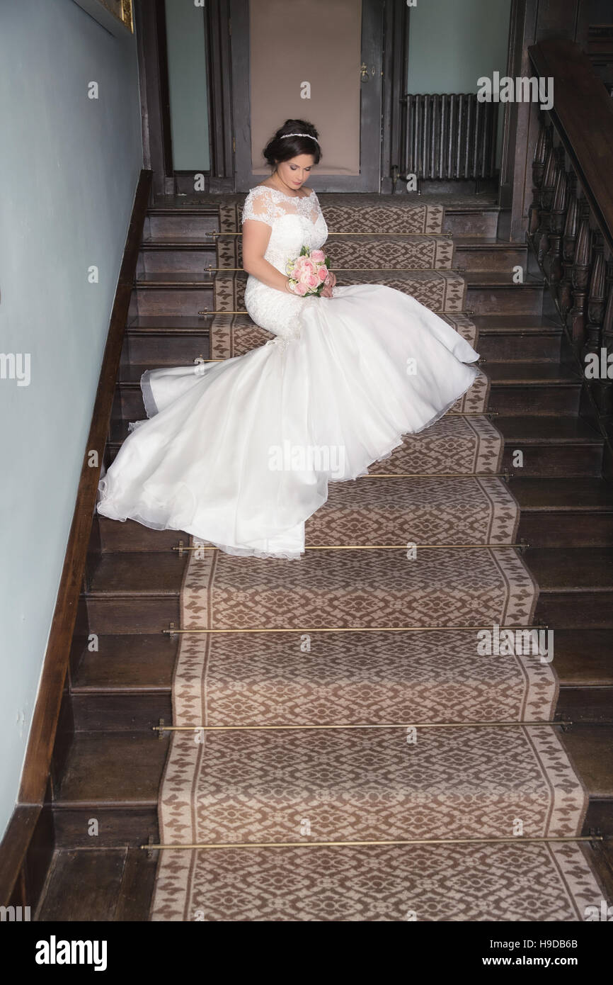 Bride sits on stairs with bridal gown flowing down the steps Stock ...