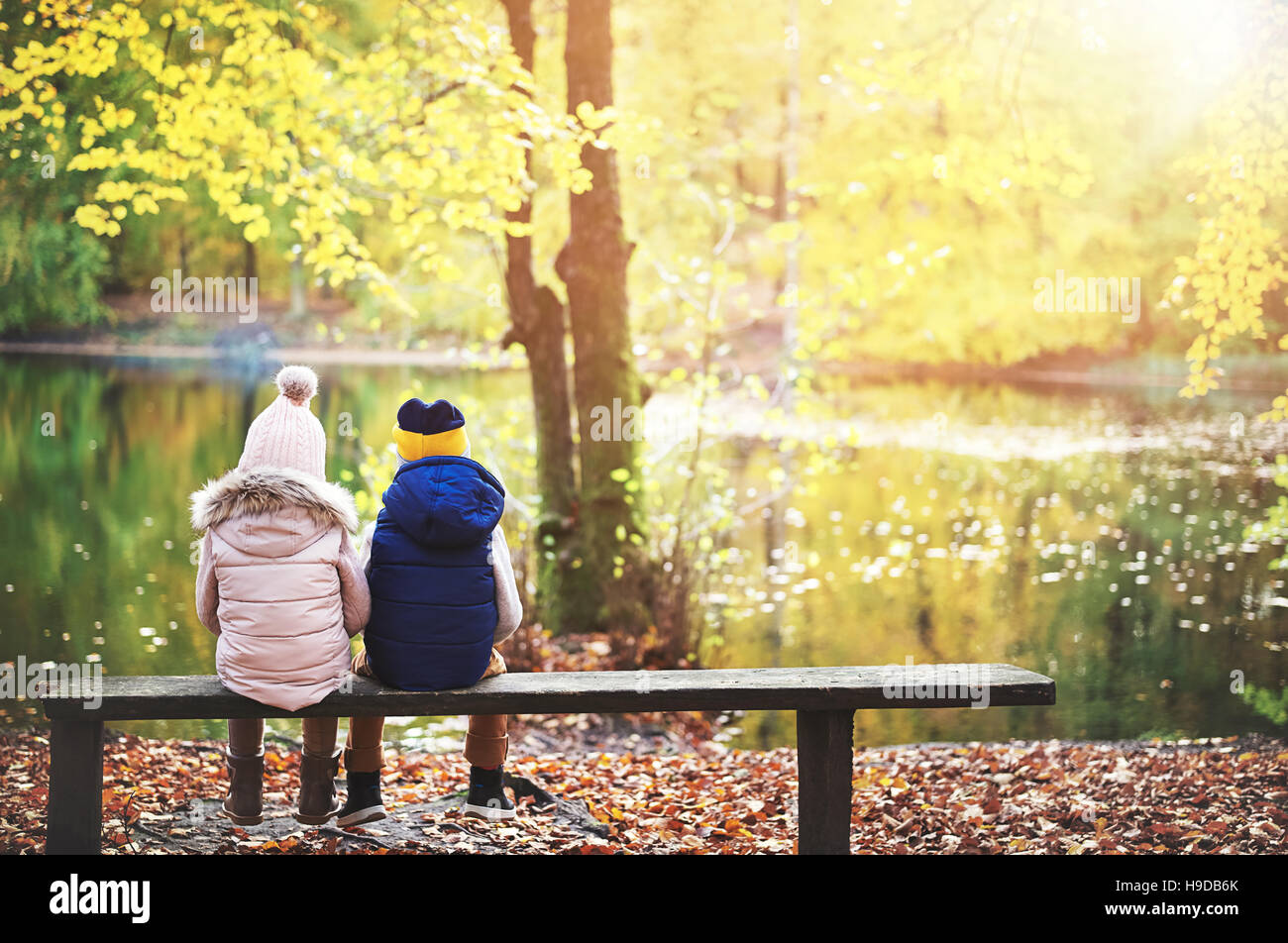 Two children on a bench in autumn forest. Horizontal outdoors shot ...