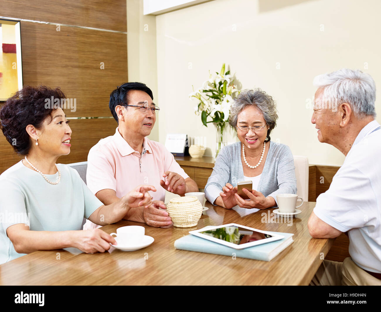 Two Senior Asian Couple Sitting Around Table Chatting At Home Stock