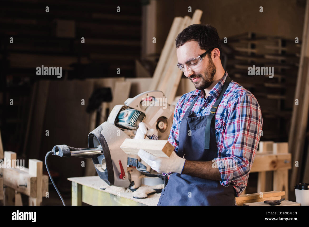 Handsome carpenter in protective glasses is looking at camera and ...