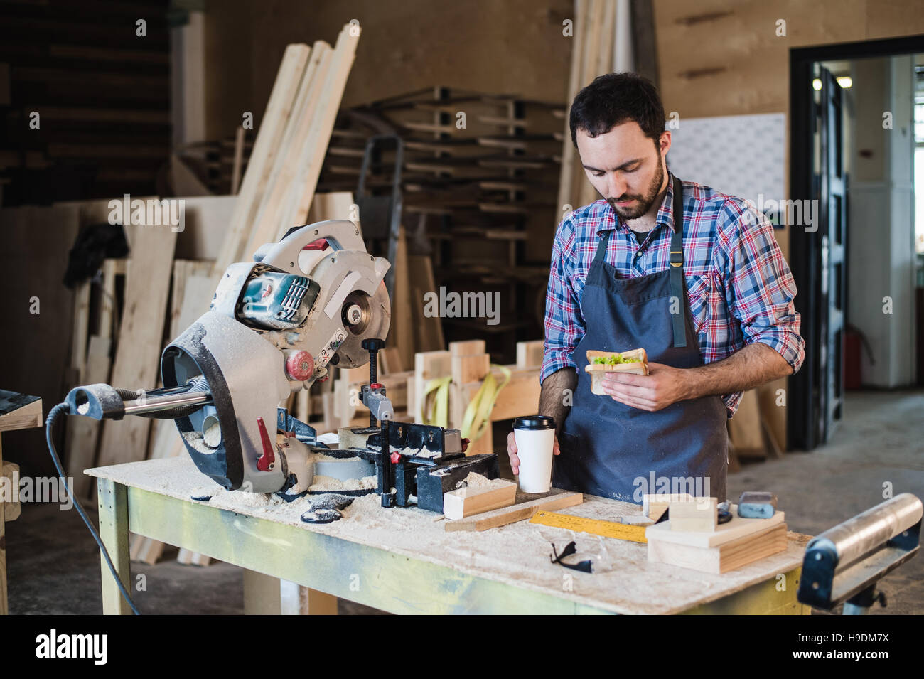 Cheerful carpentry worker having lunch eating sandwich in a workshop ...