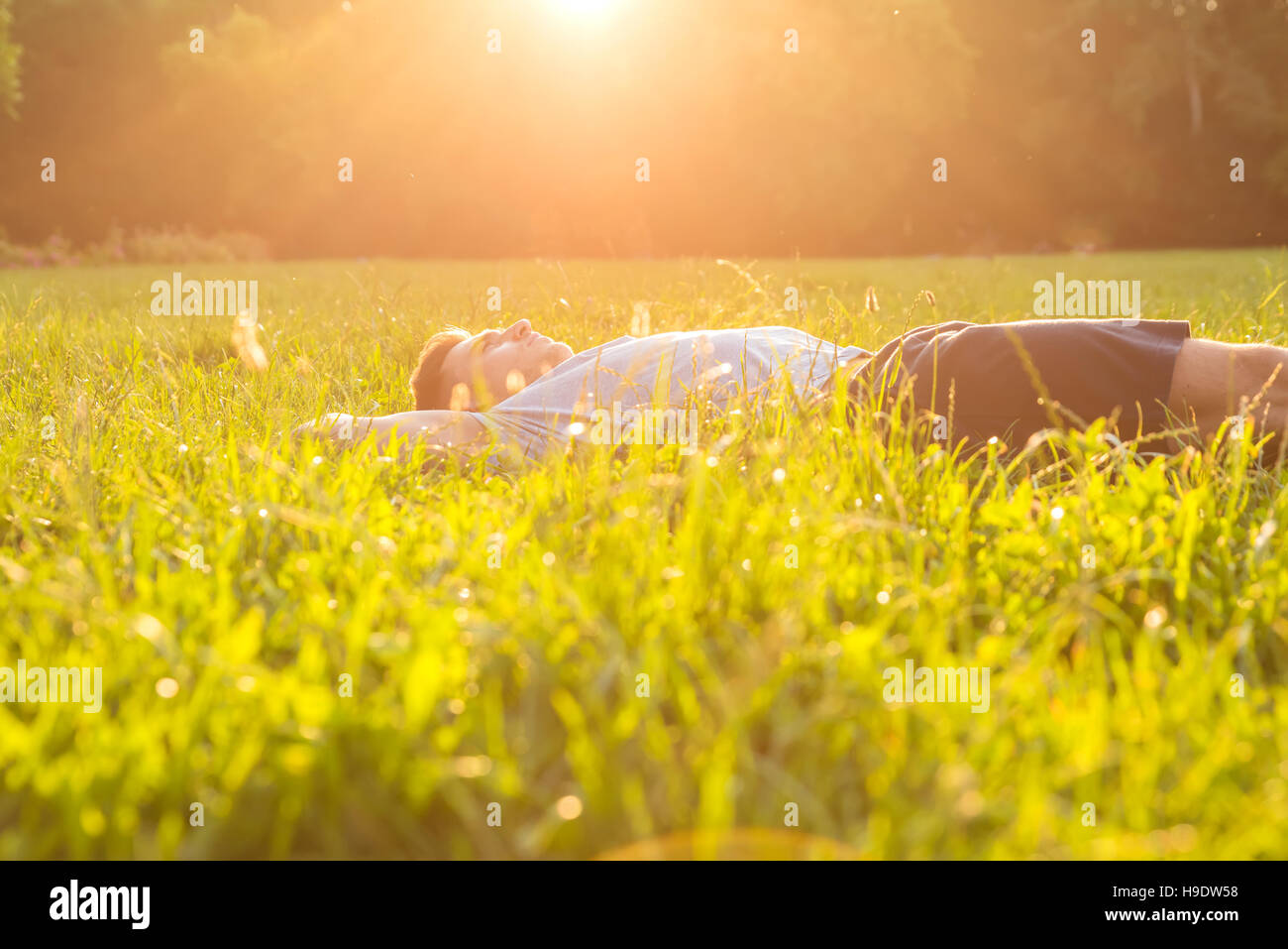 A handsome young man relaxing in the sunset and lying in the grass ...