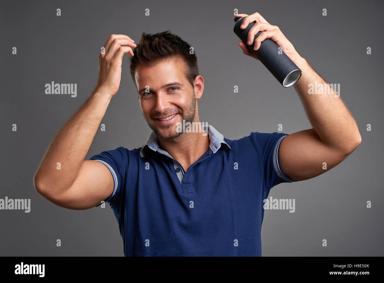 A handsome young man smiling while fixing his hair with a hairspray ...