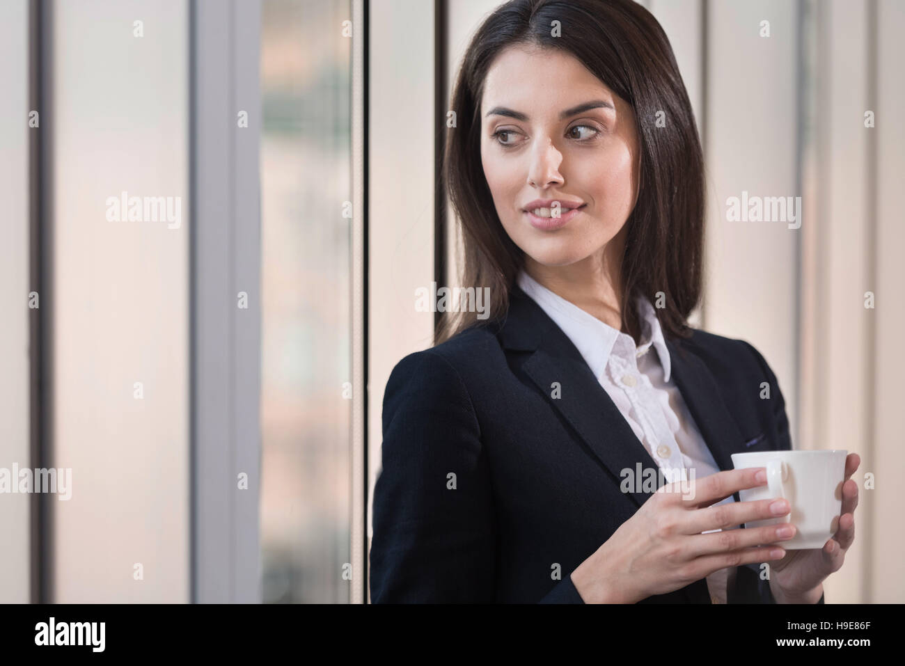 Brunette woman drinking coffee in an office Stock Photo - Alamy