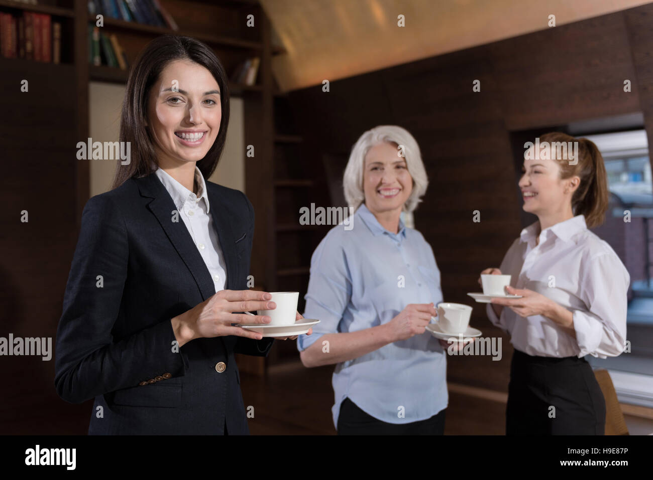 Female colleagues smiling during coffee break at workplace Stock Photo ...