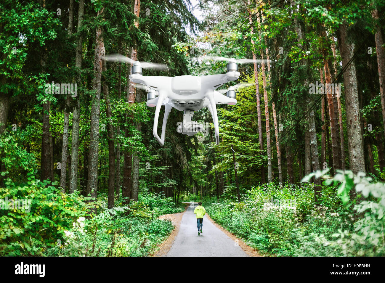 Hovering drone taking pictures of man running in forest Stock Photo - Alamy