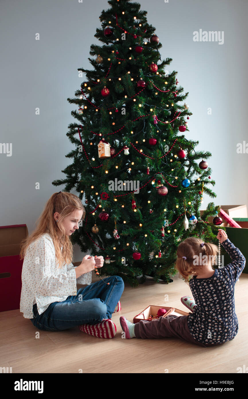 Young girl and her little sister decorating Christmas tree at home ...