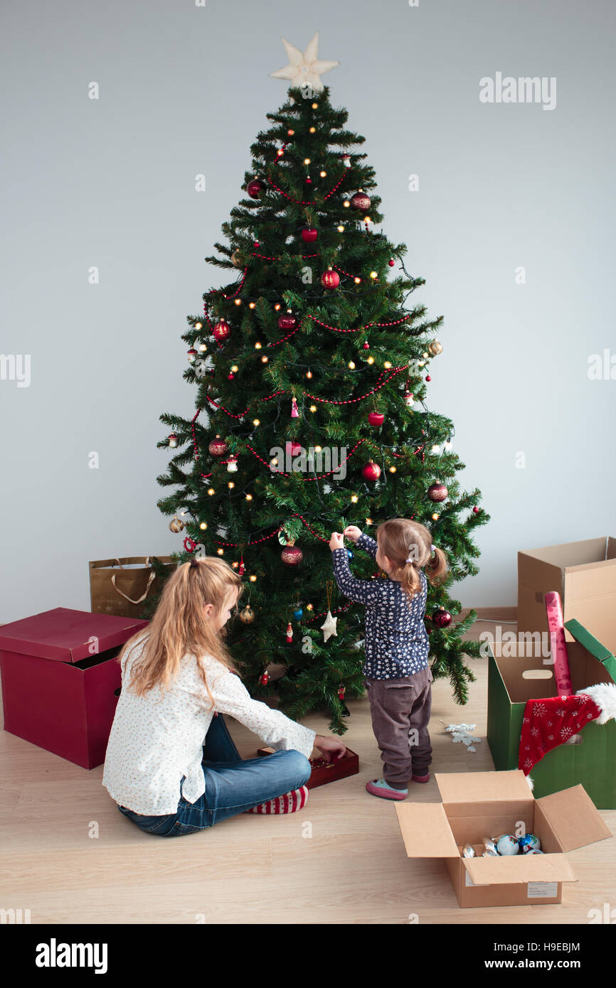 Young girl and her little sister decorating Christmas tree at home ...